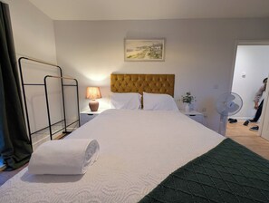 Quarto de hotel com cama grande, abajur, ventilador e quadro na parede.