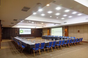 Uma sala de conferências com uma mesa comprida, cadeiras azuis e uma tela de projetor exibindo a marca 'JANNAT'.