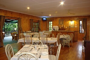 Interior de madeira com mesas preparadas para refeições, área de bar e vista para o exterior.