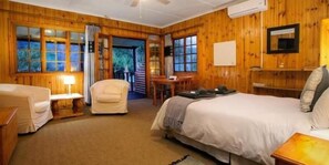 Quarto com painéis de madeira, uma cama, uma cadeira, uma escrivaninha e uma televisão.