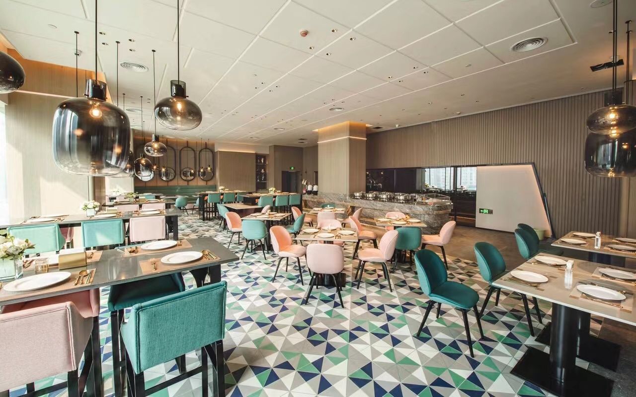 Uma sala de jantar moderna com várias mesas e cadeiras, piso estampado e iluminação pendente.