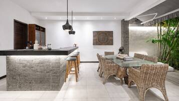 Cozinha moderna com ilha central, banquetas, mesa de jantar com cadeiras de vime e luminária pendente.