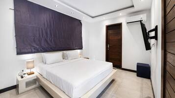 Quarto moderno com uma cama grande, mesas de cabeceira, televisão e porta de madeira.