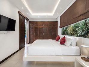 Quarto moderno com uma cama grande, TV fixada na parede e janela com vista para o verde.