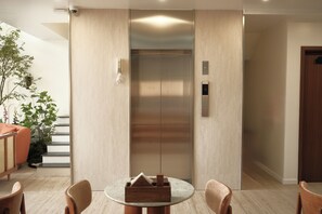 Interior moderno com elevador central, uma mesa redonda com um modelo de madeira e escada decorada com plantas.