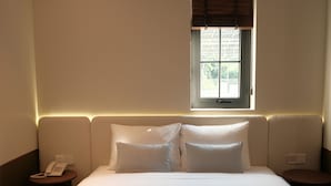 Quarto de hotel com cama, duas mesas de cabeceira, telefone e janela com persianas.