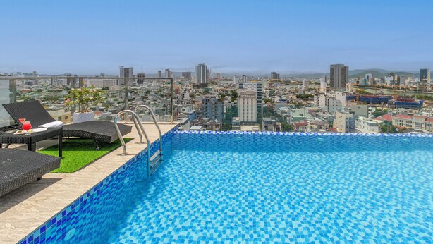 Piscina no terraço com vista para a cidade, espreguiçadeiras e céu claro.