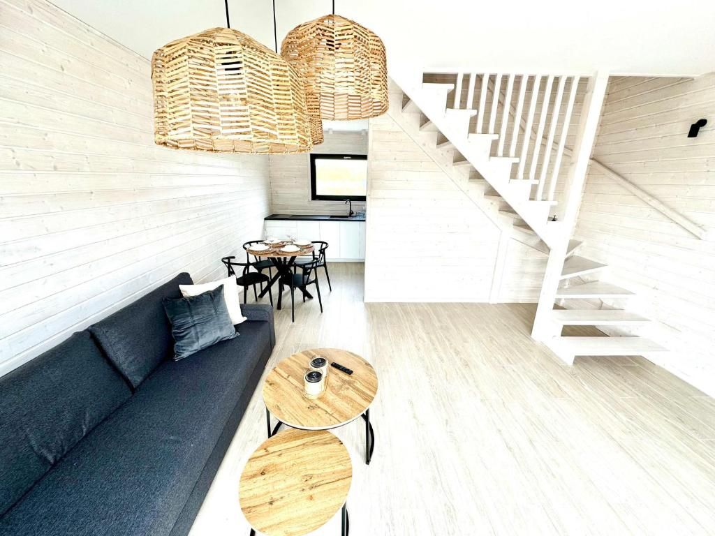 Um interior moderno com sofá, mesas de madeira redondas, luminárias pendentes de vime e uma escada.