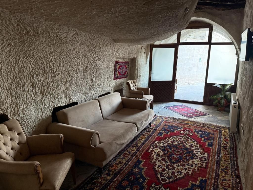 Um quarto aconchegante com parede de pedra, um sofá bege, tapete estampado e uma janela grande.