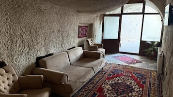Um quarto aconchegante com parede de pedra, um sofá bege, tapete estampado e uma janela grande.