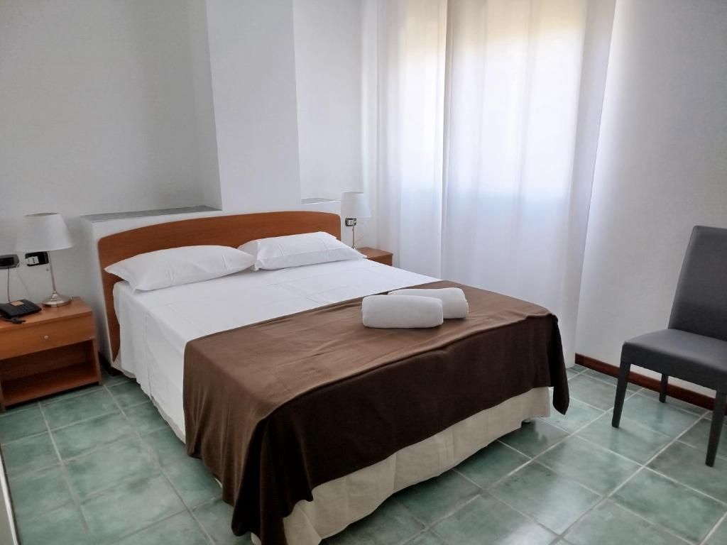 Quarto de hotel com cama, uma cadeira, mesa de cabeceira e abajur.