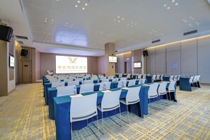Uma sala de conferências com fileiras de mesas e cadeiras, uma tela de projeção e uma placa indicando o Vienna International Hotel.