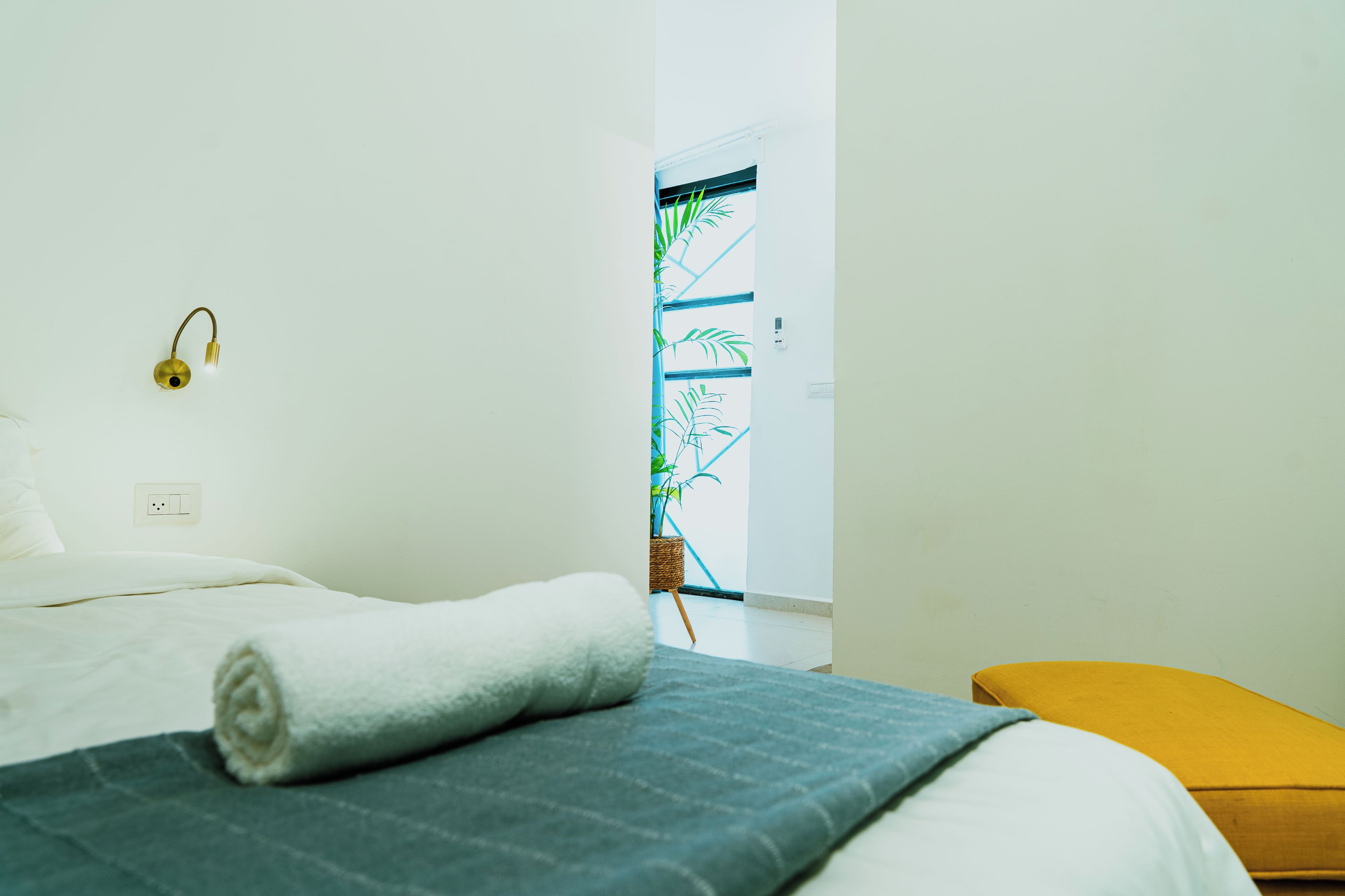 Quarto de hotel com cama, mesa de cabeceira, luminária na parede e janela com vista para o verde.