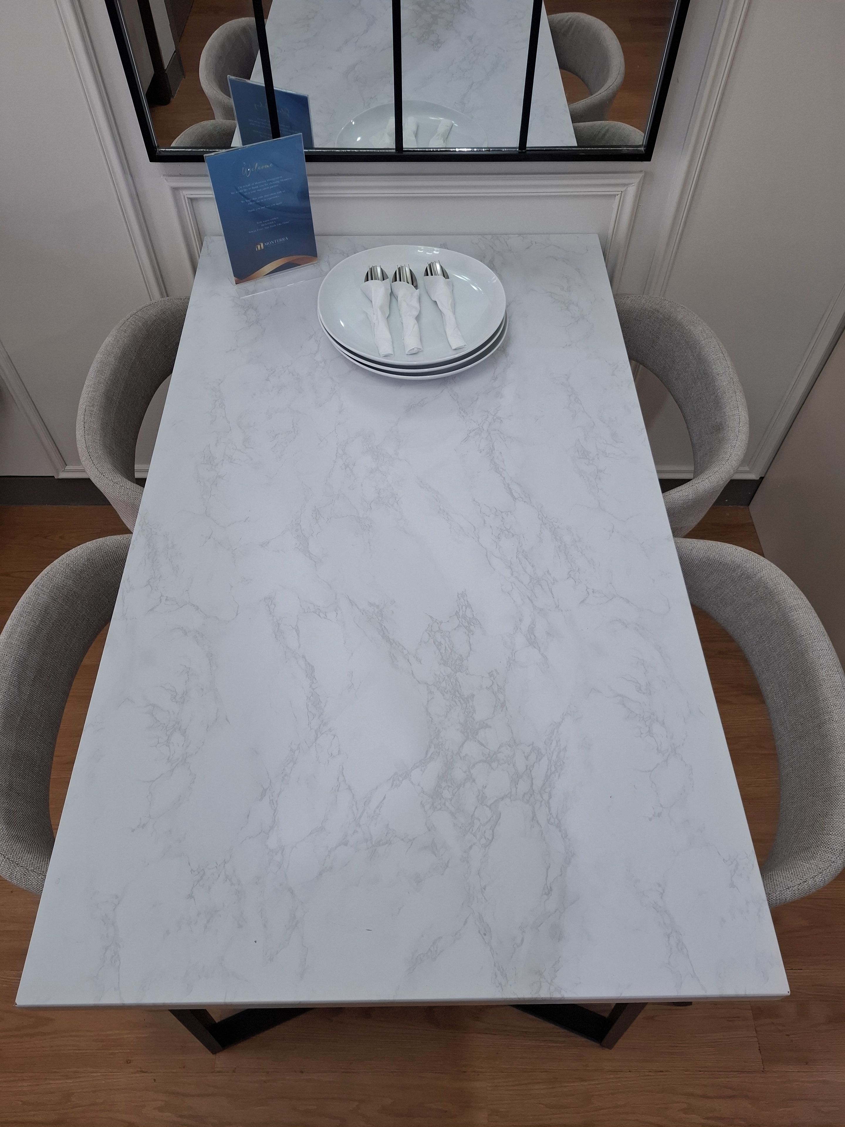 Mesa de jantar com tampo de mármore, rodeada por duas cadeiras estofadas, um conjunto de pratos e um livreto azul.