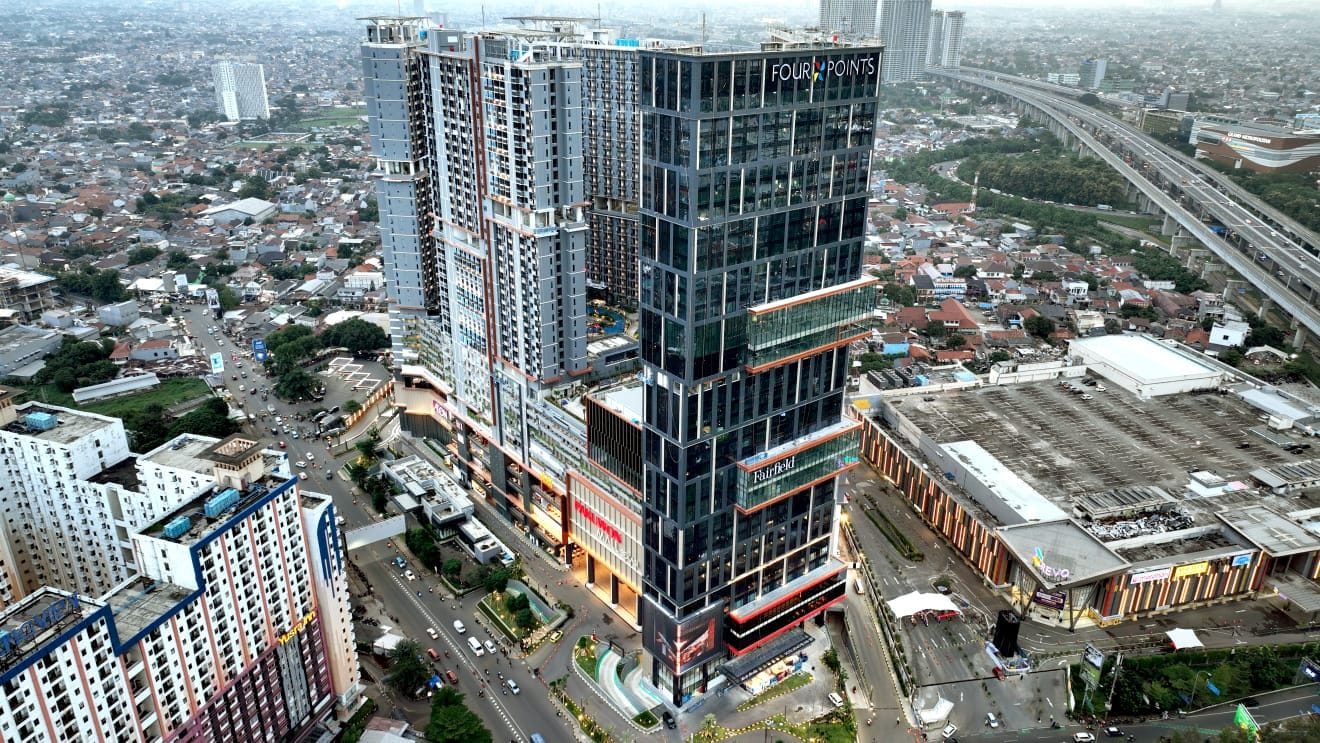 Um edifício de vários andares com fachada de vidro moderna, inserido em um ambiente urbano movimentado com ruas e outros edifícios.