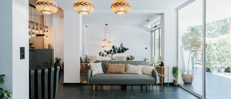 Uma sala de estar moderna com um sofá cinza, três luminárias pendentes e uma janela grande com vista para o exterior.