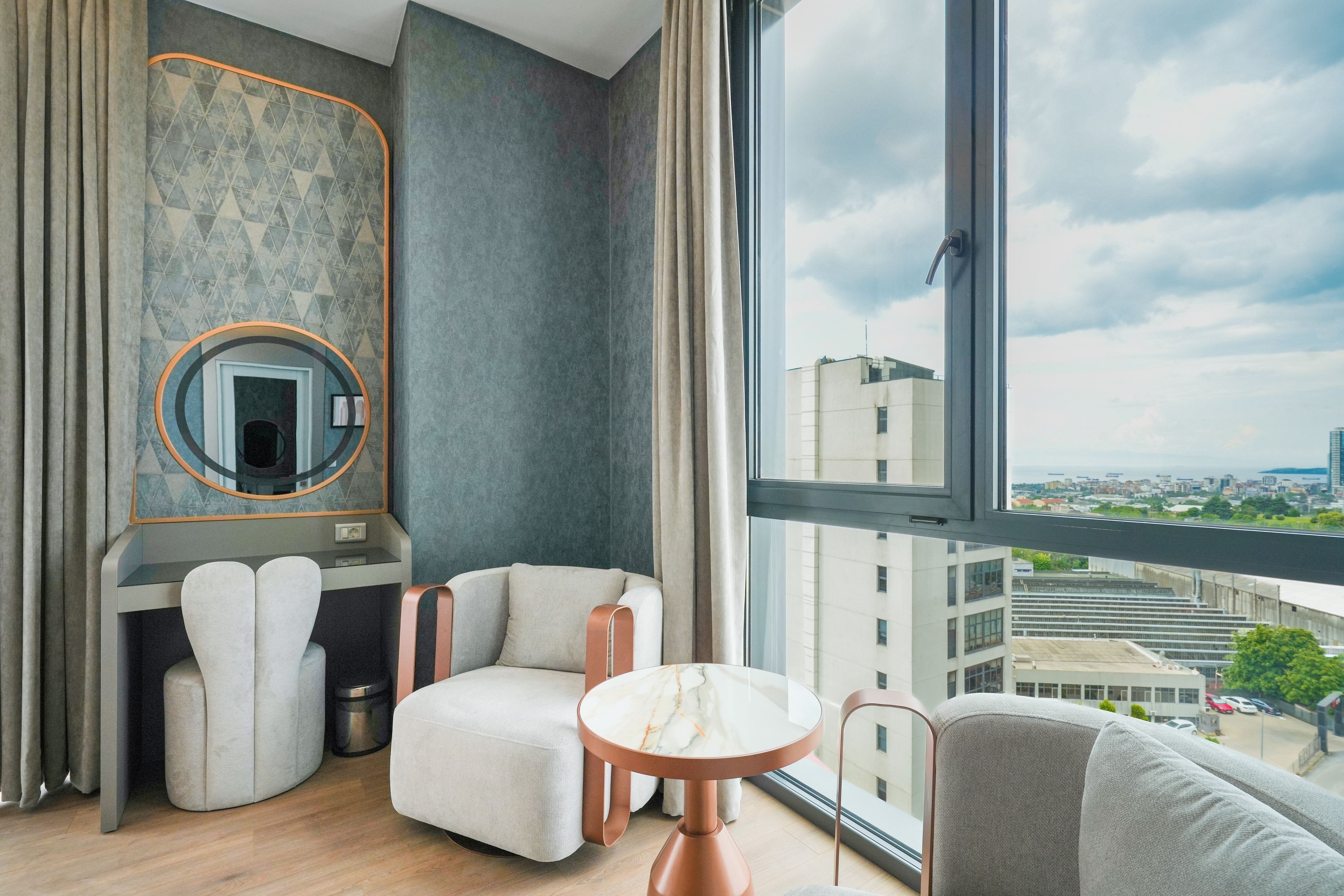 Quarto de hotel moderno com uma grande janela, um espelho redondo e uma mesa de mármore.