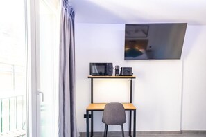 Quarto com escrivaninha, cadeira, televisão de tela plana na parede e janela com cortinas.