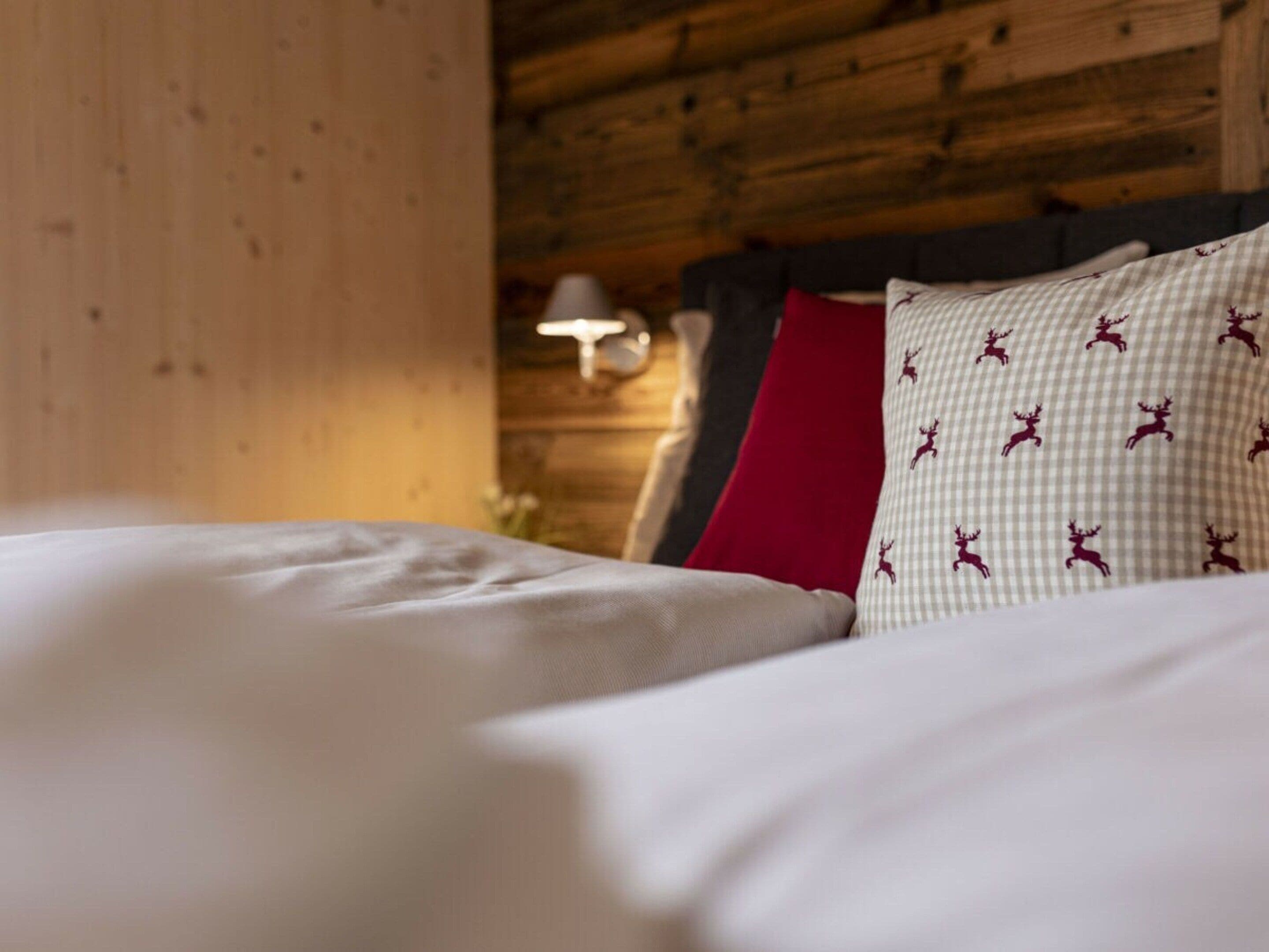 Cama com roupa de cama branca e travesseiro com padrão xadrez e desenho de veado.