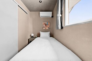 Quarto de hotel com cama, mesa de cabeceira, ar condicionado na parede, quadro e janela com cortinas.