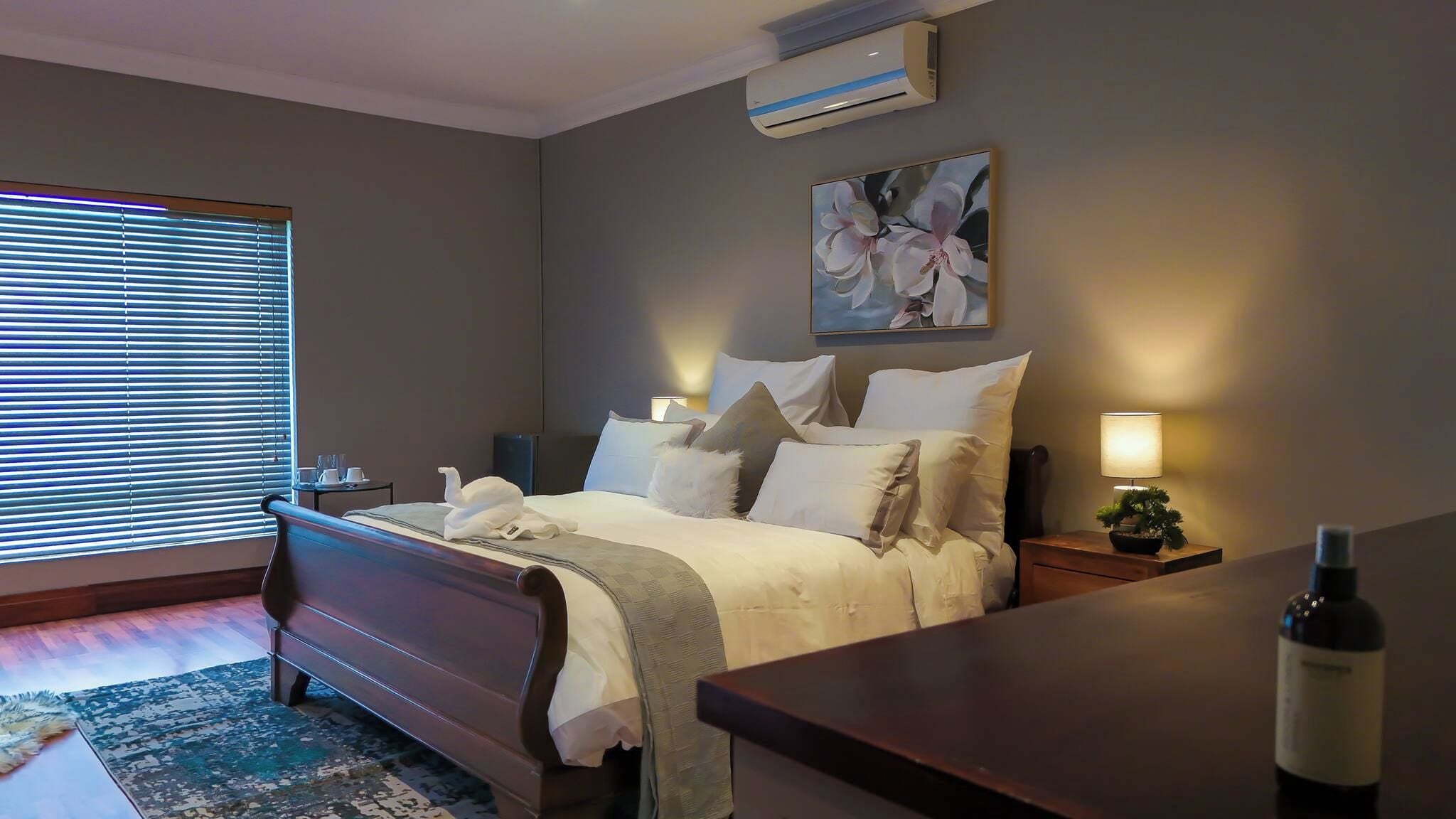 Quarto com cama, mesas de cabeceira, ar condicionado, um quadro e janela com persianas.