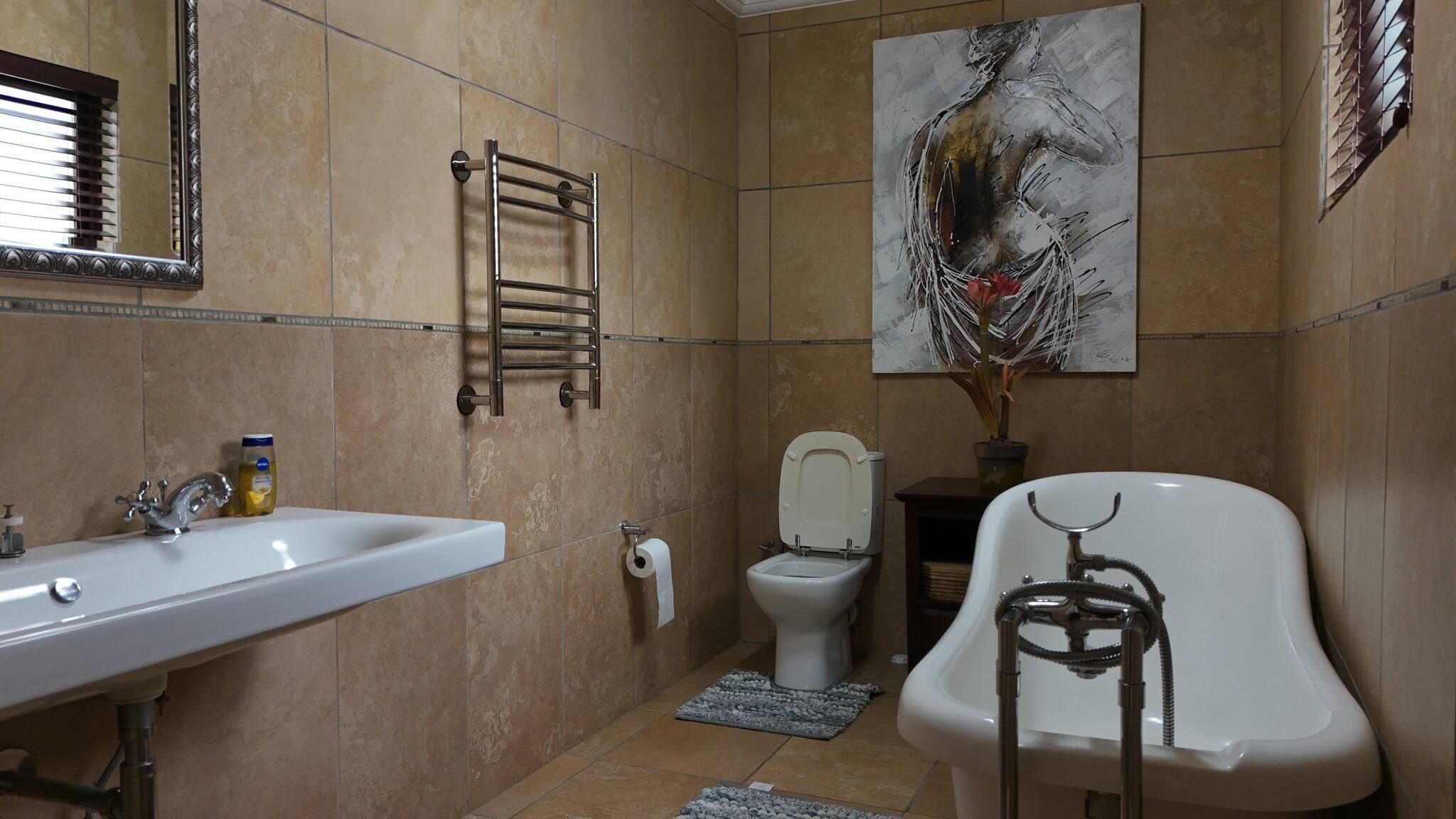 Casa de banho com uma pia branca, sanita e banheira. Há um porta-toalhas na parede e um quadro sobre a sanita.