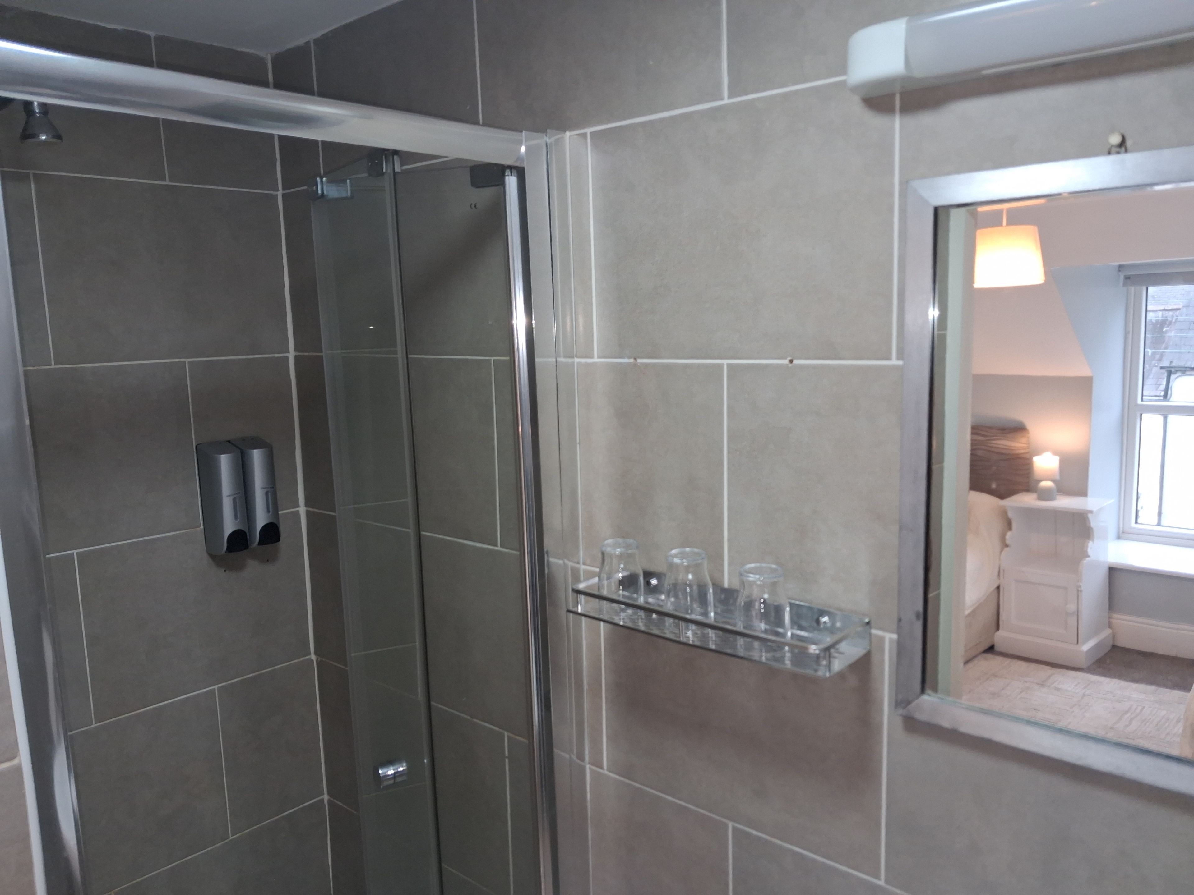 Casa de banho moderna com cabine de duche em vidro, dispensador de sabonete líquido e prateleira de vidro com produtos de higiene pessoal.