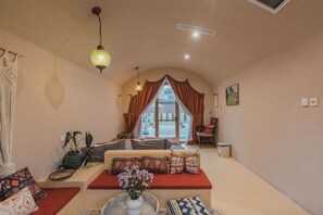 Uma sala de estar aconchegante com sofá, janela com cortinas, luminária pendente e planta no peitoril.