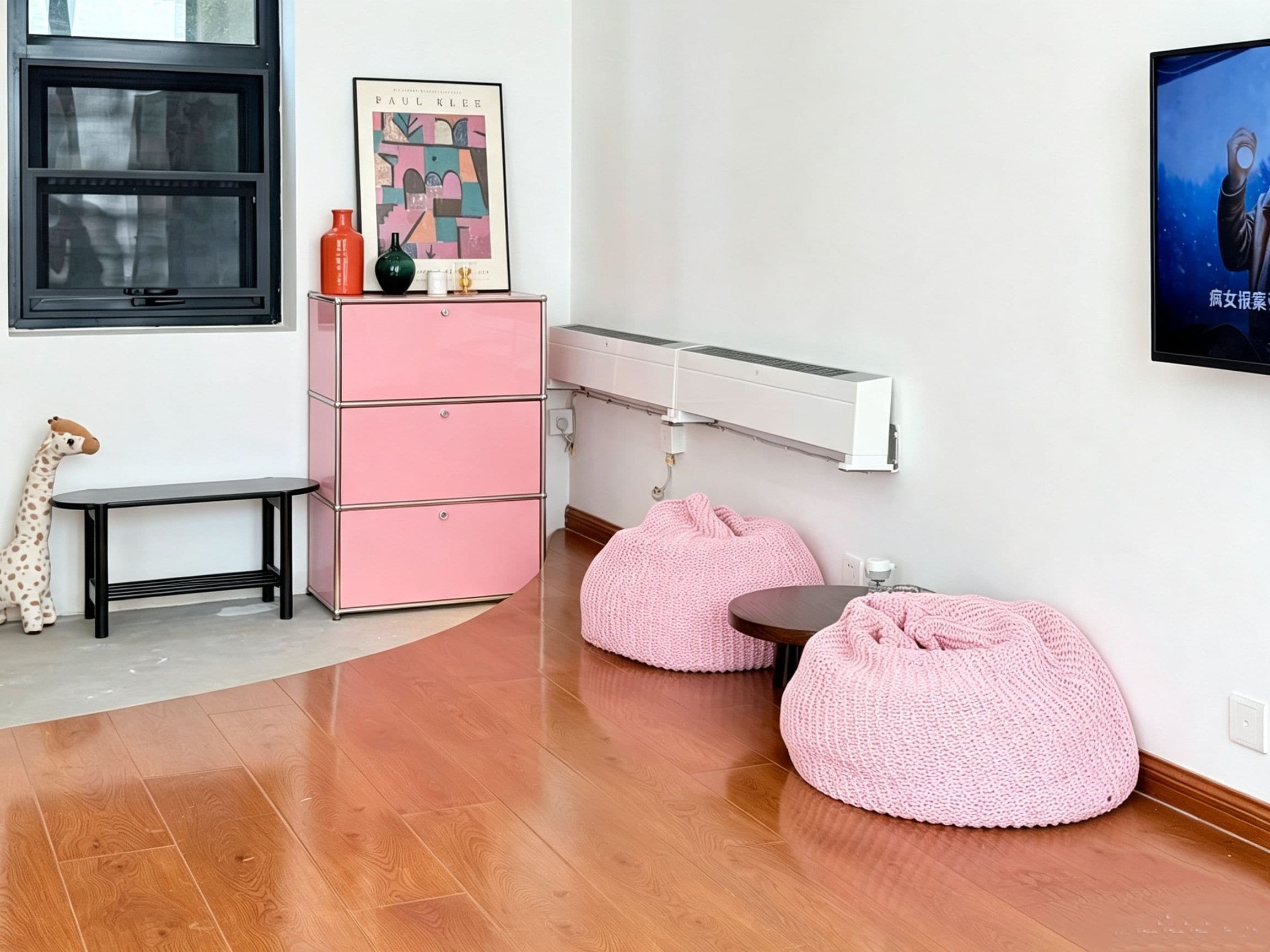 Quarto com um armário rosa, um banco, dois sacos de feijão, um radiador e uma obra de arte emoldurada na parede.