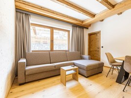Uma sala de estar moderna com um sofá seccional, uma pequena mesa de madeira e uma área de jantar com cadeiras.