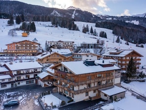Estância de esqui coberta de neve, com vários edifícios no estilo chalé, um teleférico e montanhas ao fundo.
