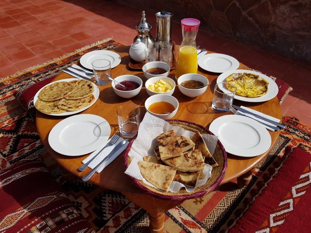 Uma mesa de café da manhã com pratos, tigelas e uma cesta de pão sírio.