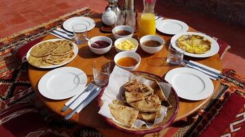 Uma mesa de café da manhã com pratos, tigelas e uma cesta de pão sírio.