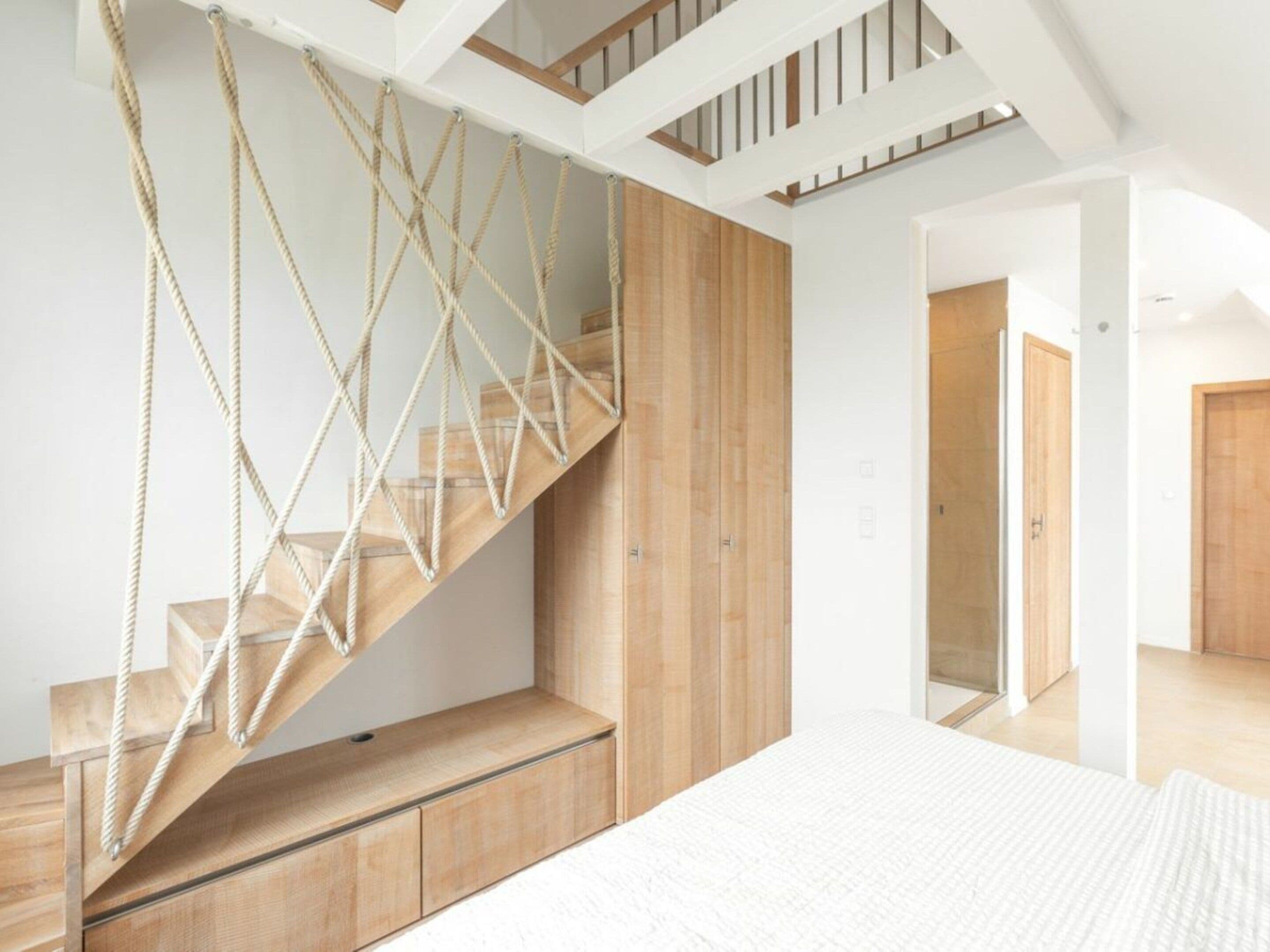 Quarto moderno com escada de madeira, roupeiro embutido e uma cama.