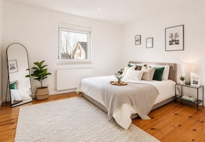 Quarto com cama, mesa de cabeceira, espelho, janela e planta.