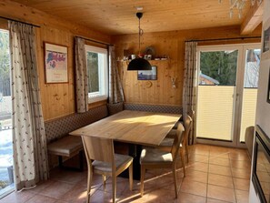 Interior de madeira com uma mesa grande e bancos, uma luminária no teto e um quadro pendurado na parede.