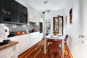 Cozinha moderna com armários brancos, coifa preta e área de refeições com mesa de madeira e cadeiras vermelhas.