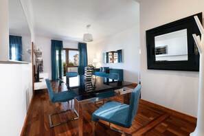 Uma área de refeições moderna com mesa de vidro, cadeiras estofadas em azul e vista para o exterior.