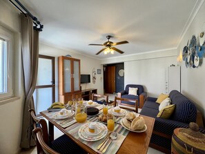 Uma sala de jantar com mesa posta para o café da manhã, um ventilador de teto e um sofá com almofadas.