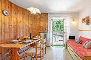 Interior em madeira com mesa de jantar posta, cama com roupa de cama vermelha e vista por uma porta.