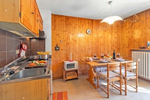 Cozinha com armários de madeira, micro-ondas e sala de jantar com mesa e cadeiras.