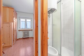 Casa de banho com chuveiro, sanita e janela com cortinas.