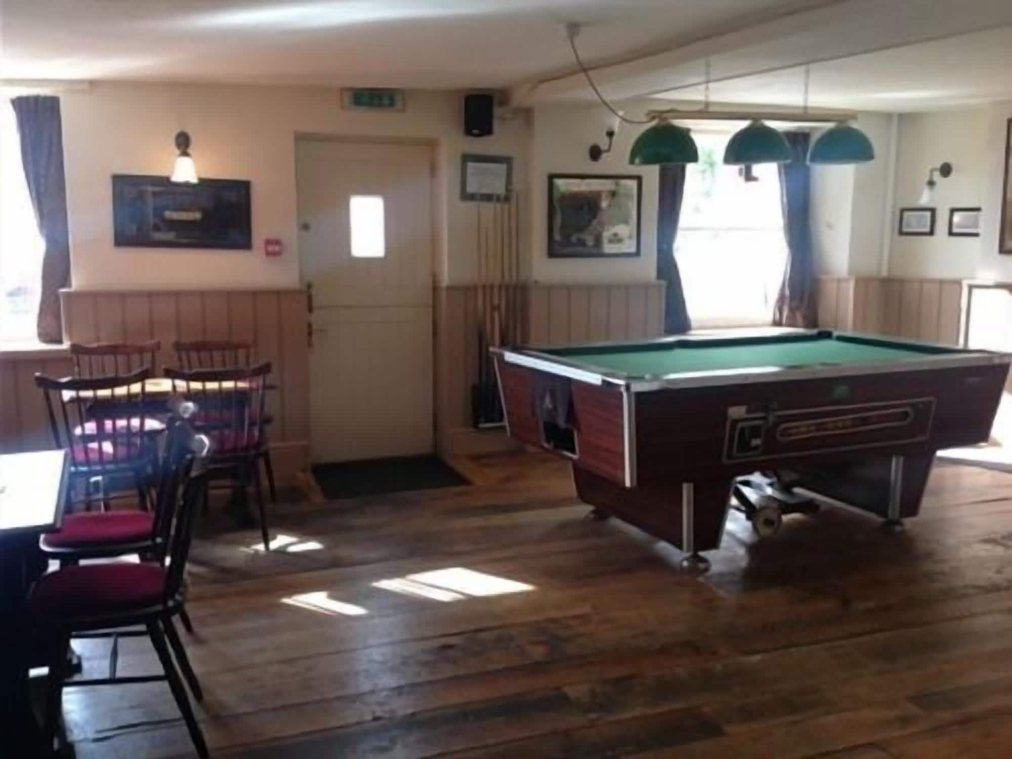 Uma mesa de bilhar em um ambiente com piso de madeira, uma porta e uma janela com cortinas.