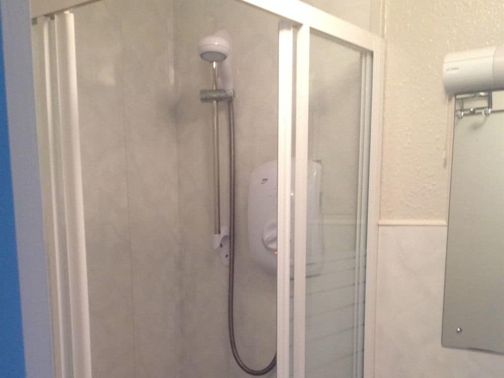 Box de chuveiro com porta de vidro, chuveiro manual e painel de controle fixado na parede.