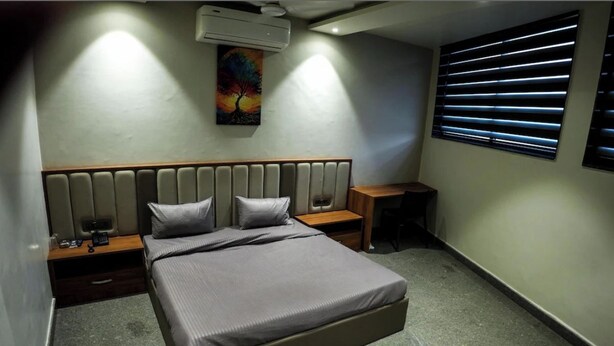 Quarto com cama, mesas de cabeceira, ar-condicionado, um quadro e janela com persianas.