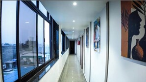 Um corredor com grandes janelas, obras de arte nas paredes e vista para a paisagem urbana.