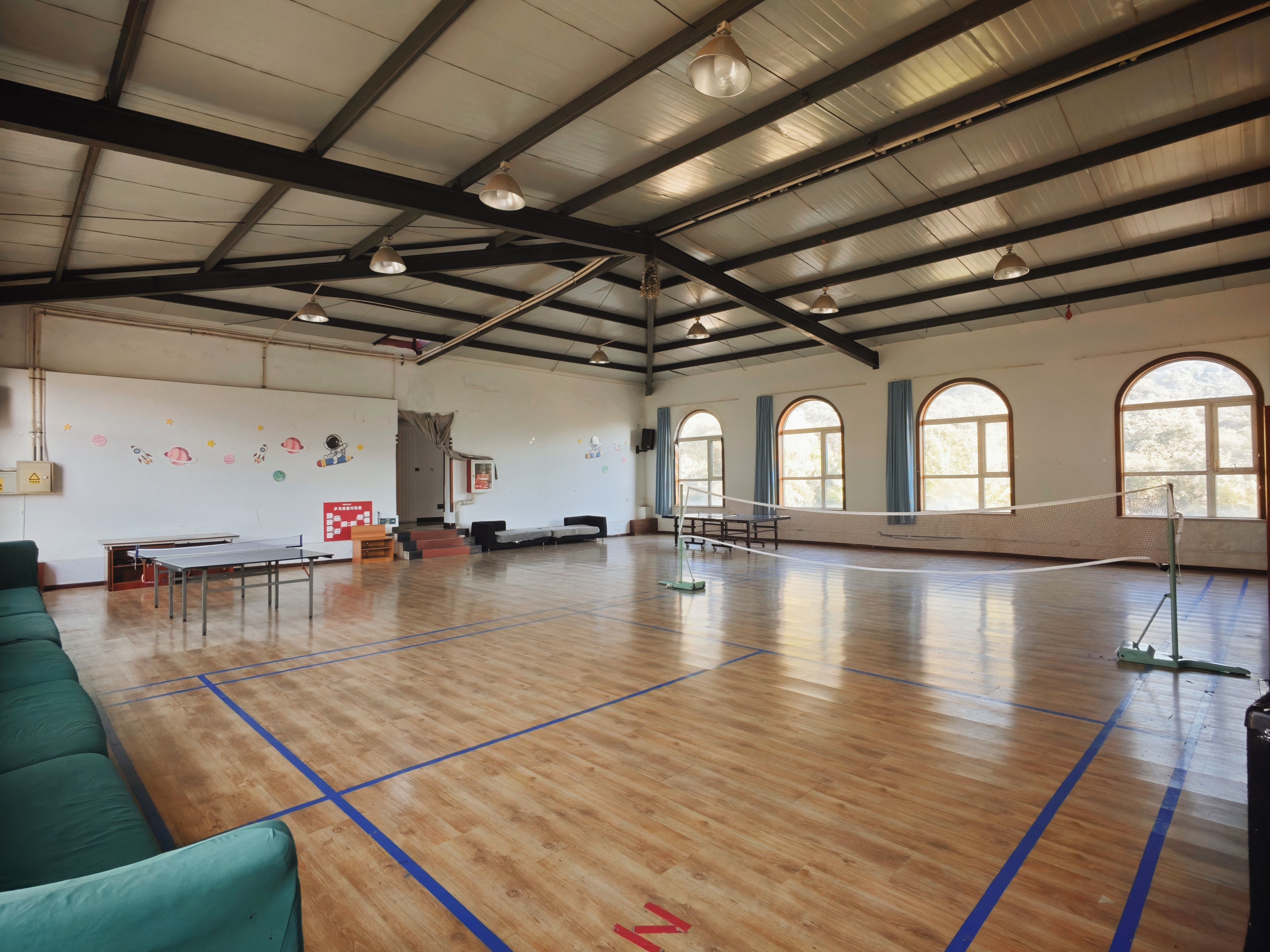 Amplo espaço interno com teto alto, piso de madeira e uma rede de voleibol.