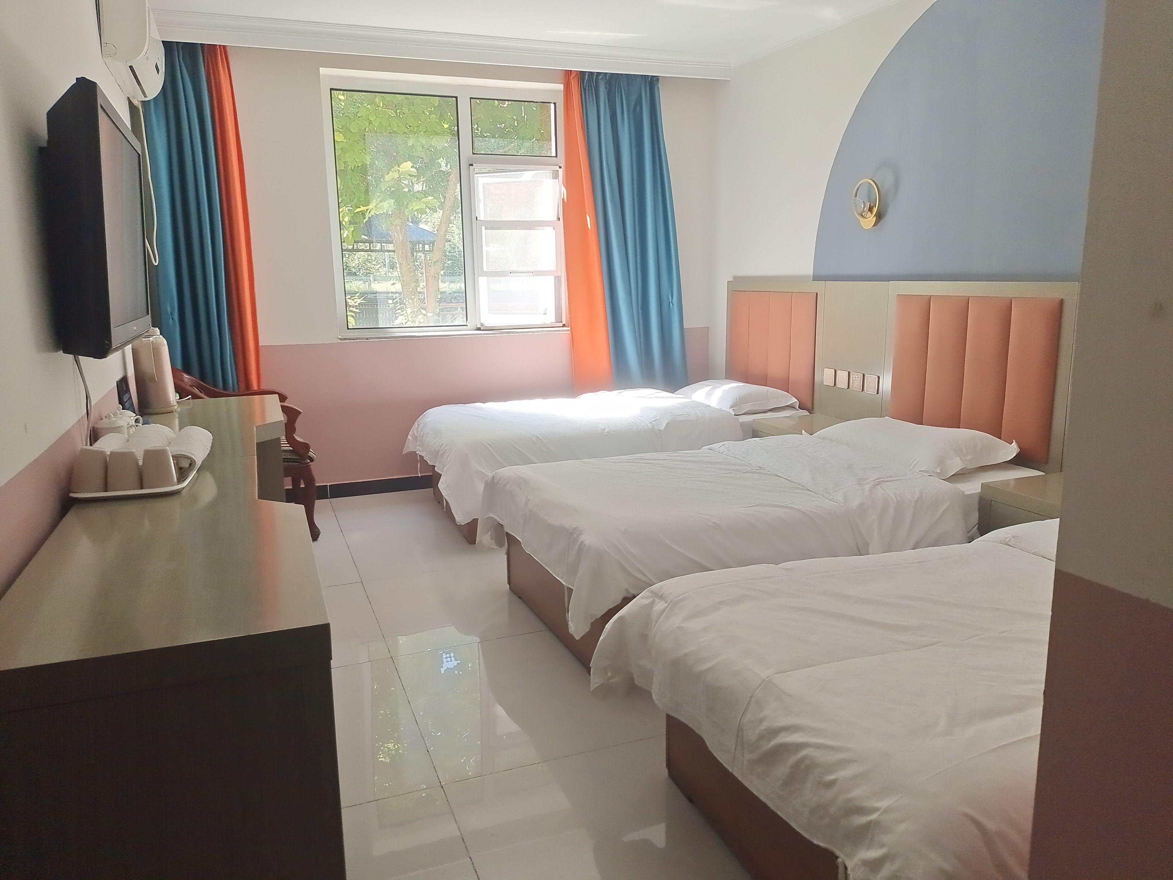 Quarto de hotel com duas camas, uma mesa de trabalho e telefone, e uma janela com cortinas.