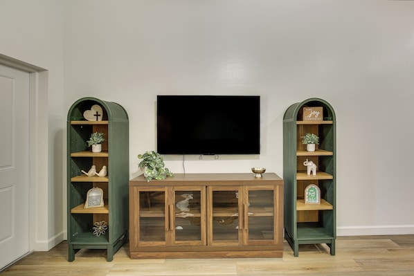 Quarto com armário de madeira, duas prateleiras verdes, uma TV de tela plana e uma pequena mesa.