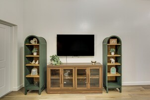 Quarto com armário de madeira, duas prateleiras verdes, uma TV de tela plana e uma pequena mesa.